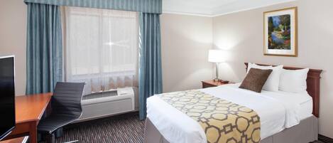 Quarto de hotel com uma cama, uma escrivaninha com cadeira, televisão, luminária e um quadro na parede.