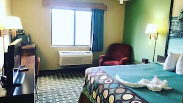 Quarto de hotel com cama, escrivaninha, cadeira, ar condicionado e janela com cortinas.