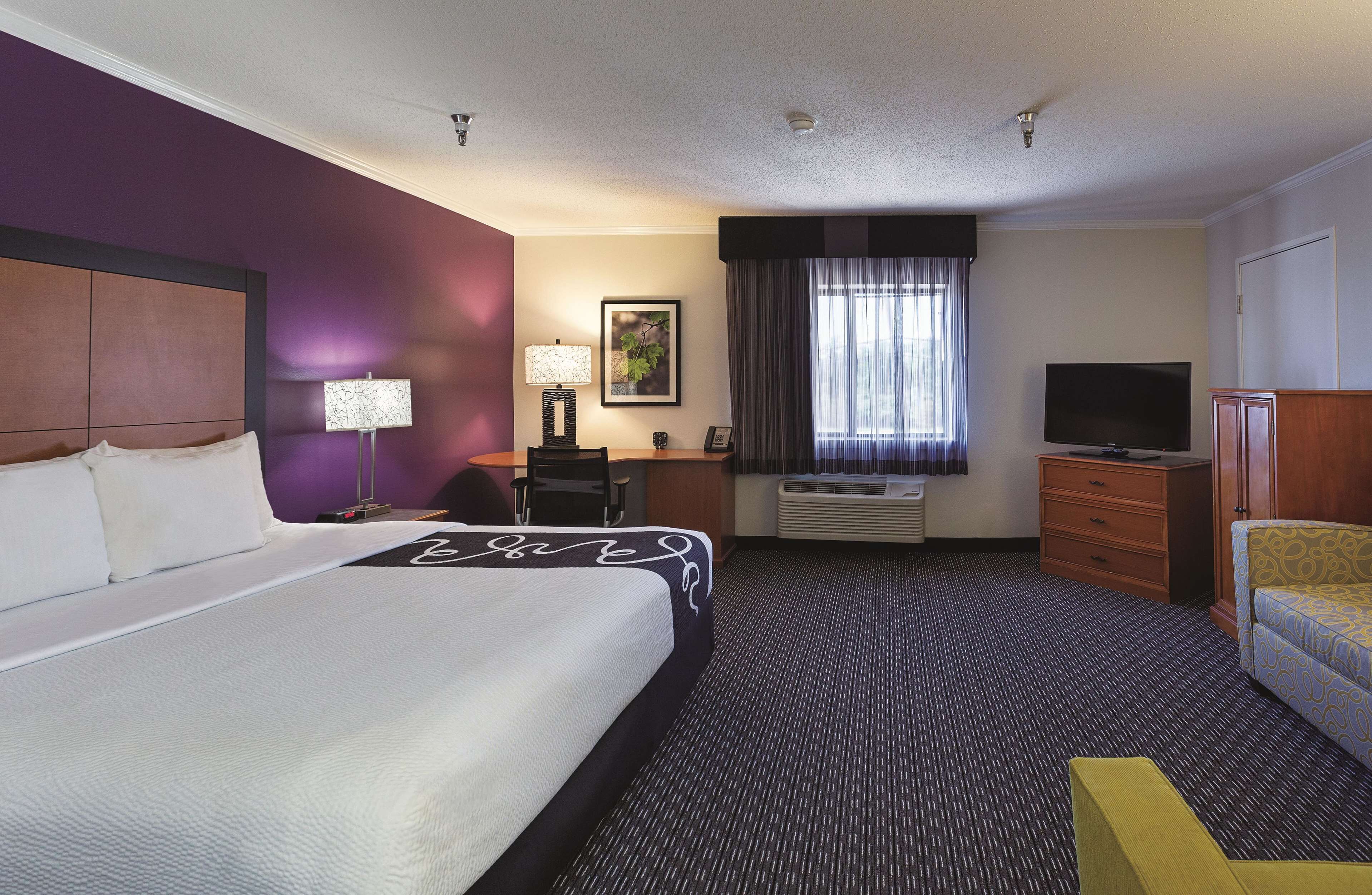 Quarto de hotel com uma cama grande, uma escrivaninha com cadeira, televisão e sofá.