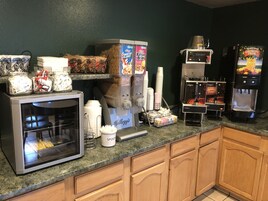 Uma cozinha equipada com geladeira, máquina de café e dispensador de bebidas.