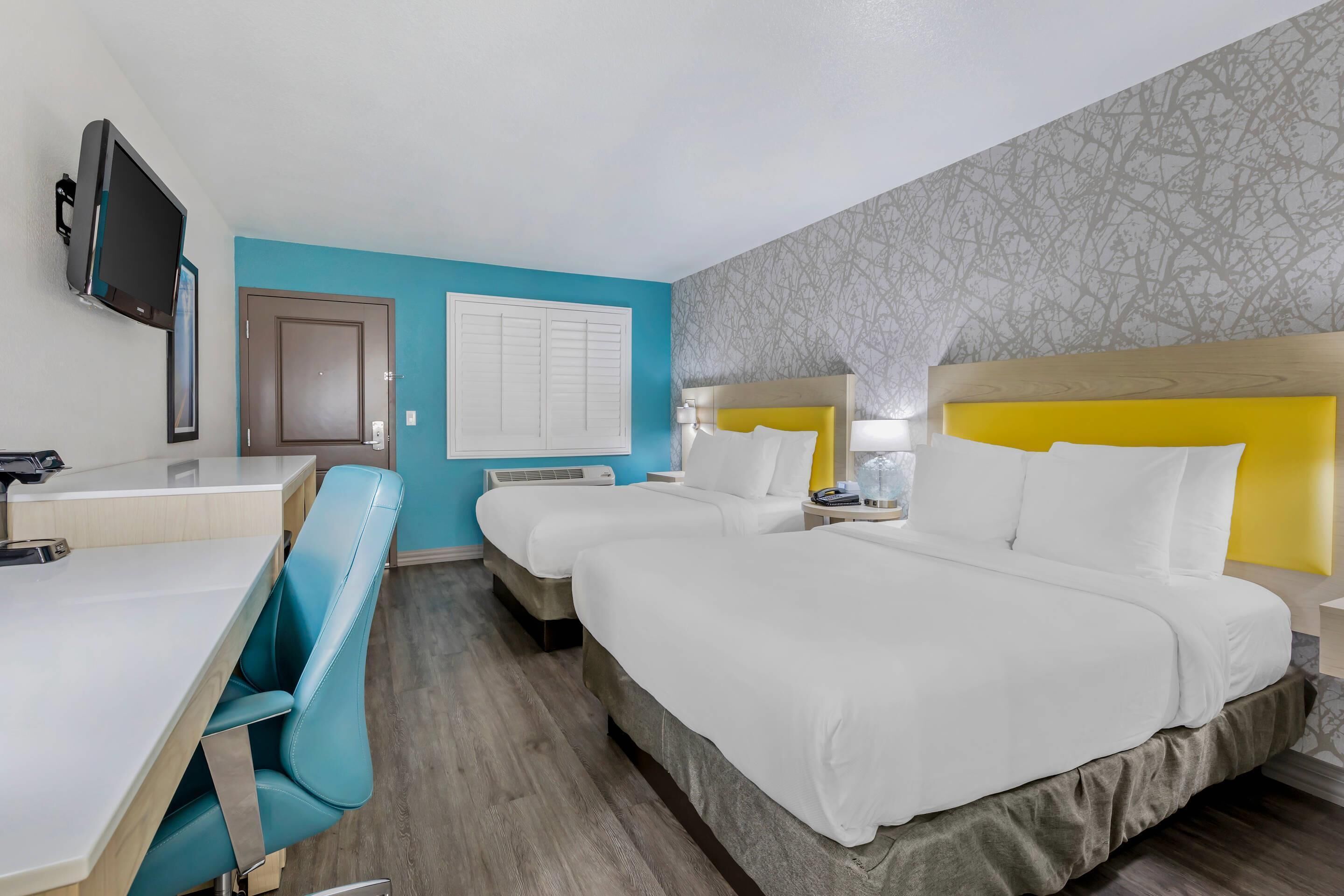 Quarto de hotel com escrivaninha, duas camas, televisão e parede estampada.