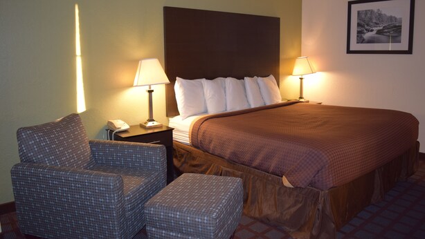 Quarto de hotel com uma cama grande, duas luminárias de cabeceira, uma cadeira e uma mesinha com um telefone.