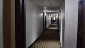 Um corredor de hotel comprido e estreito, com portas em ambos os lados, carpete estampado e teto com iluminação embutida.