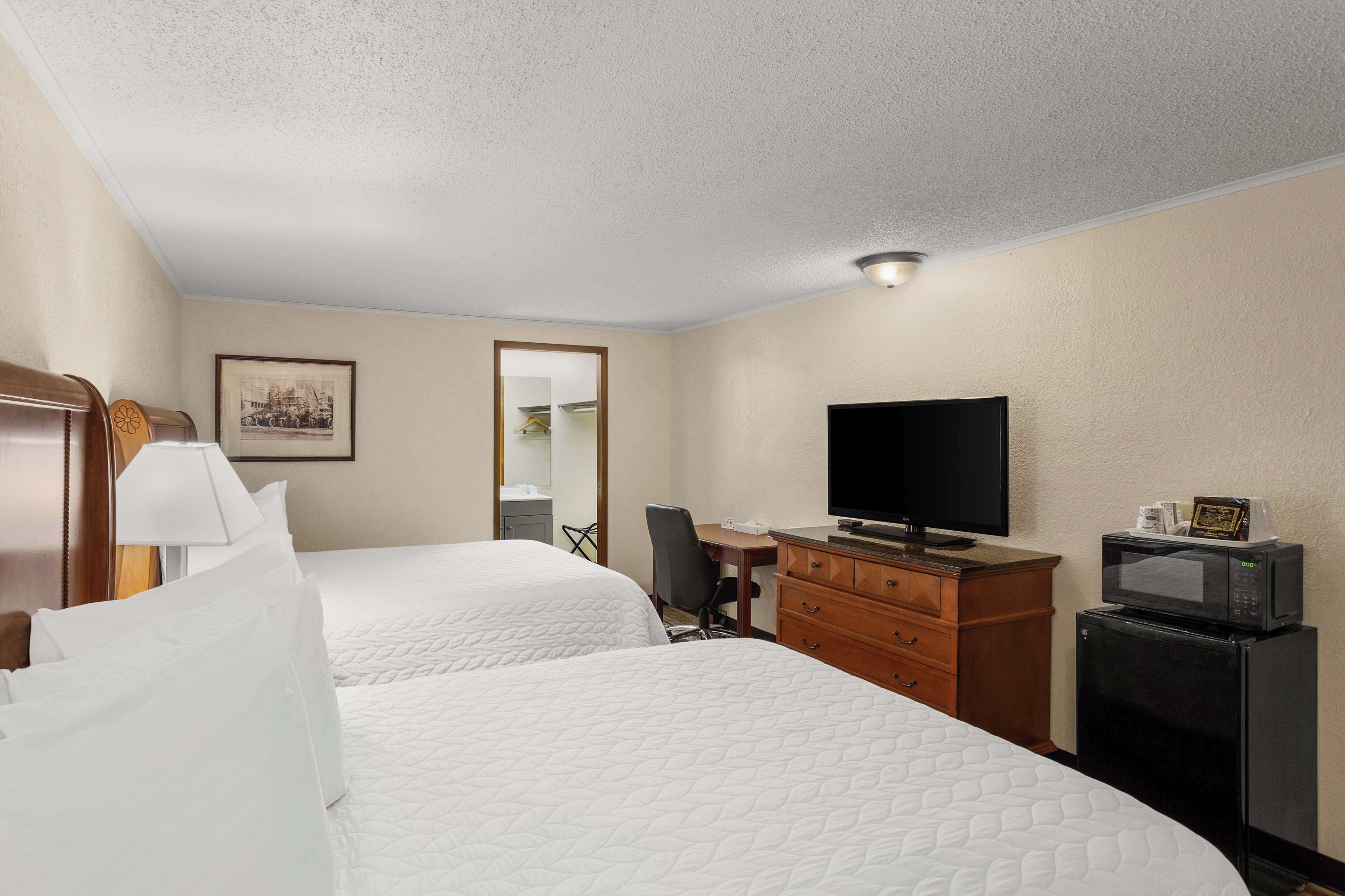 Quarto de hotel com duas camas, uma escrivaninha, televisão, frigorífico e espelho.