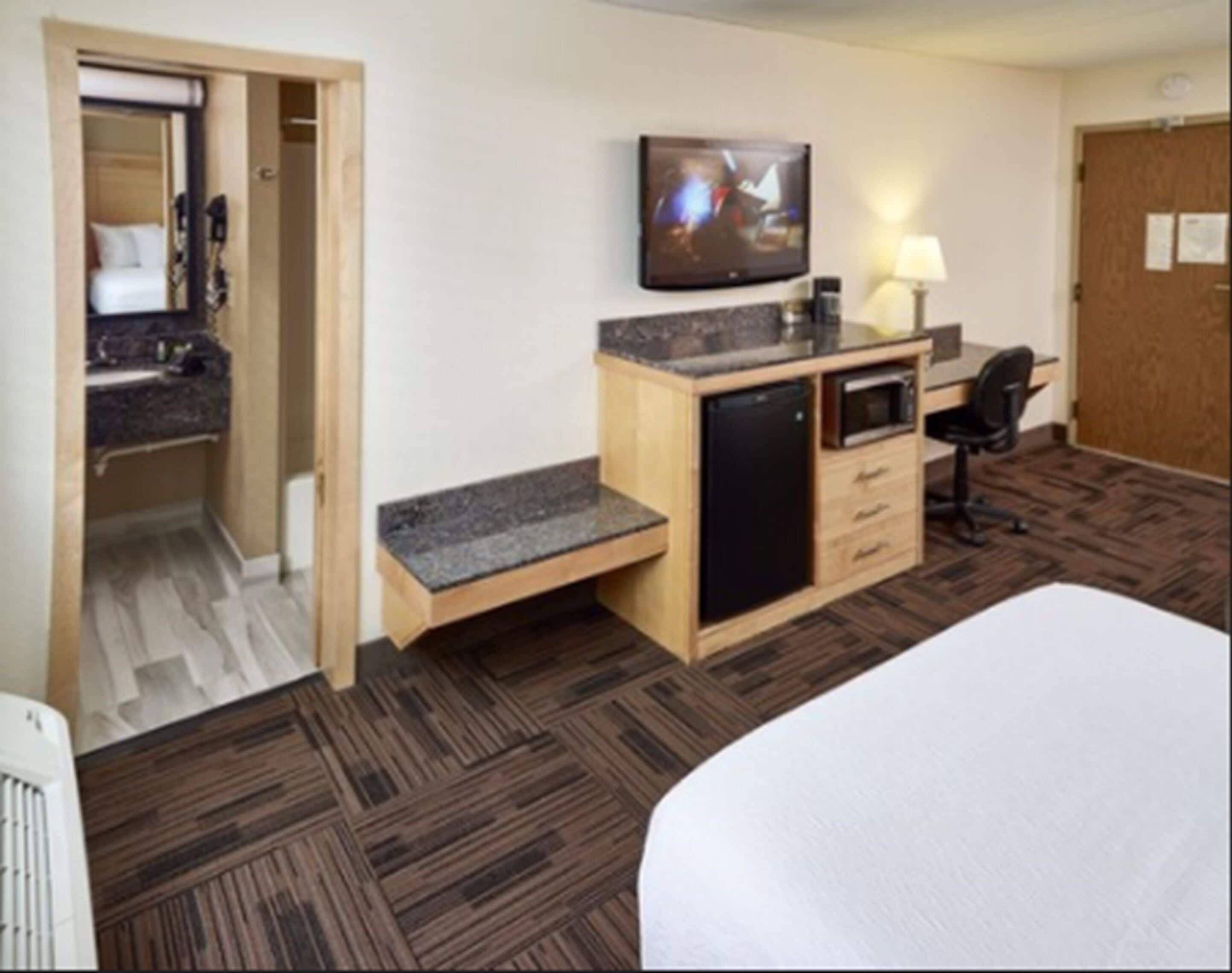 Quarto de hotel com cama, escrivaninha com computador, micro-ondas e televisão.