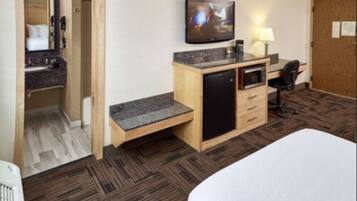 Quarto de hotel com cama, escrivaninha com computador, micro-ondas e televisão.