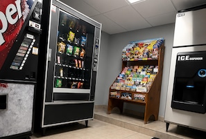 Uma área com máquinas de venda automática, variedade de lanches e uma seleção de revistas.