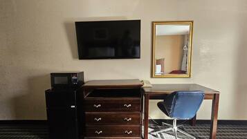 Quarto de hotel com escrivaninha de madeira, uma cadeira, televisão, micro-ondas e espelho.