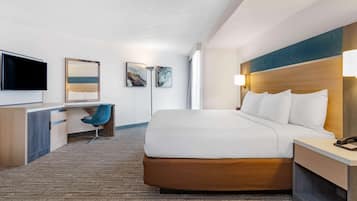 Quarto de hotel com cama, escrivaninha, cadeira, televisão e obras de arte nas paredes.