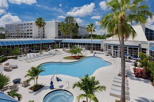 Área de piscina de resort com espreguiçadeiras, palmeiras e uma grande piscina.