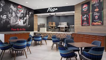 Interior de restaurante com temática de pizza, apresentando um balcão, área de estar e quadros de cardápio.