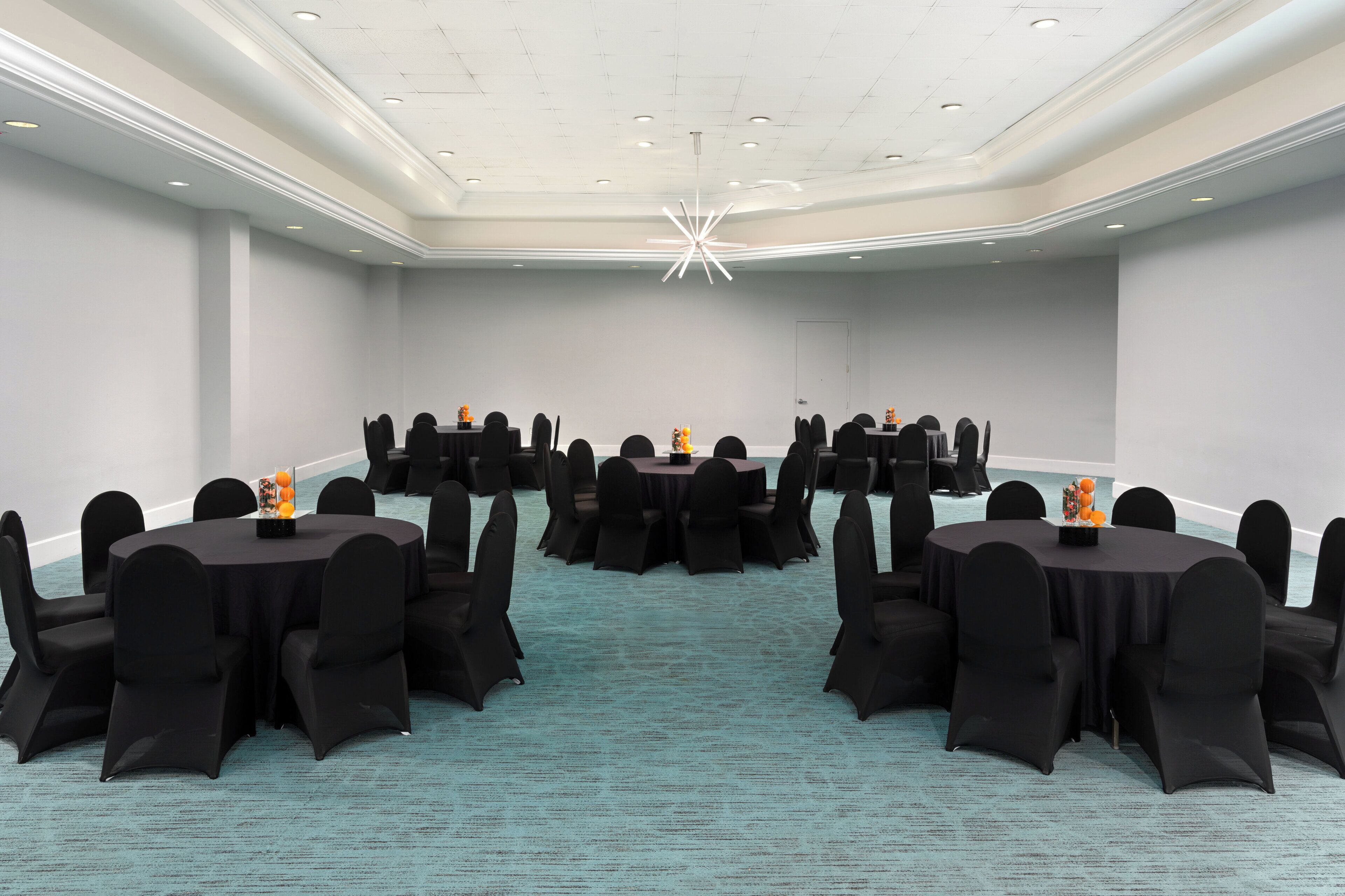 Sala de conferências com mesas redondas, cadeiras pretas e um tapete azul.