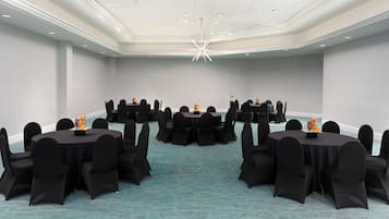 Sala de conferências com mesas redondas, cadeiras pretas e um tapete azul.