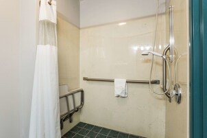 Uma área de chuveiro com porta de vidro, barra de apoio, porta-toalhas e chuveiro.