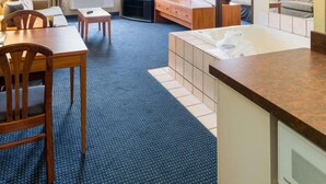 Quarto de hotel com área de refeições, televisão, sofá, mesa pequena, escrivaninha e banheira.