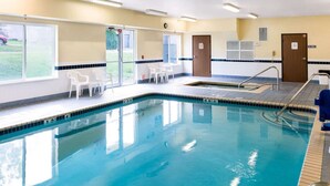 Piscina interior com água cristalina, um deck ladrilhado e algumas cadeiras brancas.