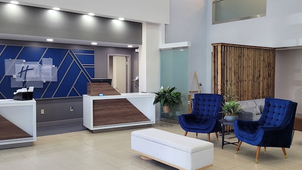 Uma área de recepção de hotel com design moderno, destacando um balcão de atendimento, cadeiras estofadas em azul e um banco branco.