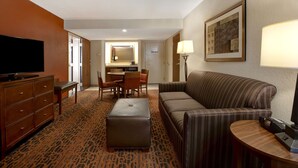 Quarto de hotel com sofá, banquinho, televisão, cómoda de madeira e área de refeições com cadeiras e mesa.