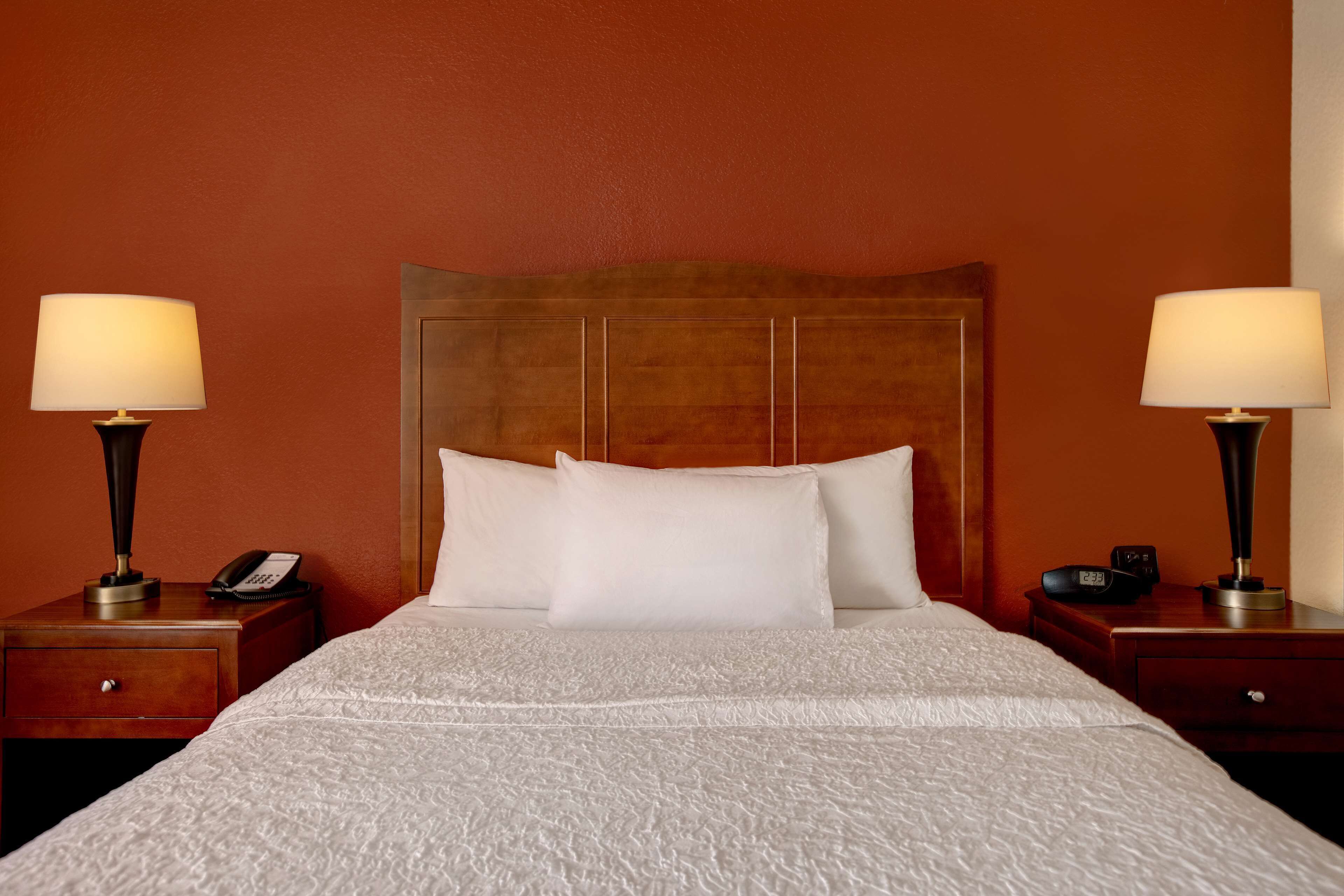 Quarto de hotel com uma cama grande, duas mesas de cabeceira, um painel de cama de madeira e duas luminárias.