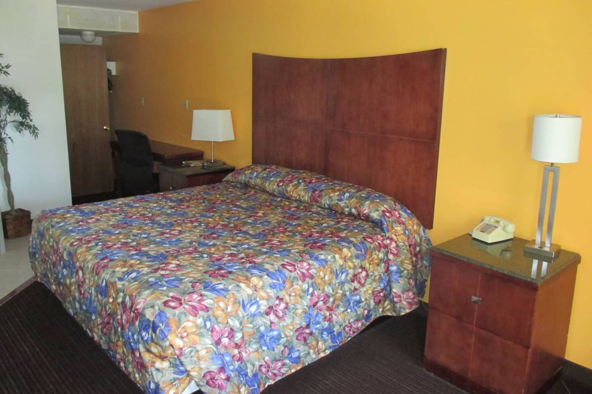Quarto de hotel com uma cama, escrivaninha, cadeira, luminária e telefone.