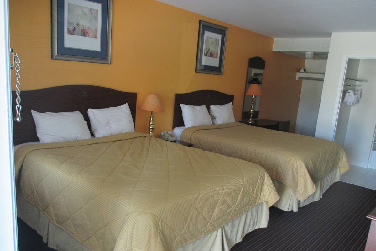 Quarto de hotel com duas camas, cada uma com cabeceira, luminária e quadro na parede.