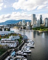 Uma marina com vários barcos atracados, cercada por edifícios modernos e uma ponte ao fundo.
