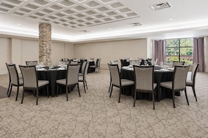 Sala de conferências com mesas redondas, cadeiras e um pilar de pedra.