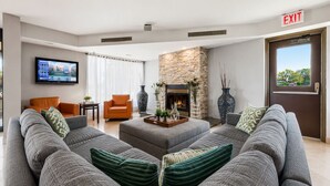 Uma sala de estar moderna com um sofá cinzento grande, uma poltrona laranja, lareira e uma televisão de tela plana fixada na parede.