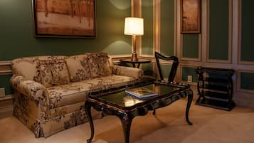 Uma sala de estar com um sofá estampado, uma mesa de centro de vidro, uma luminária e obras de arte emolduradas nas paredes.