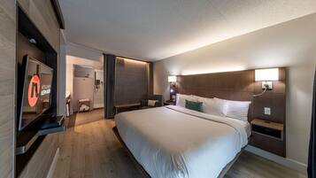 Quarto de hotel moderno com uma cama grande, mesas de cabeceira, televisão e banheiro visível por uma porta aberta.