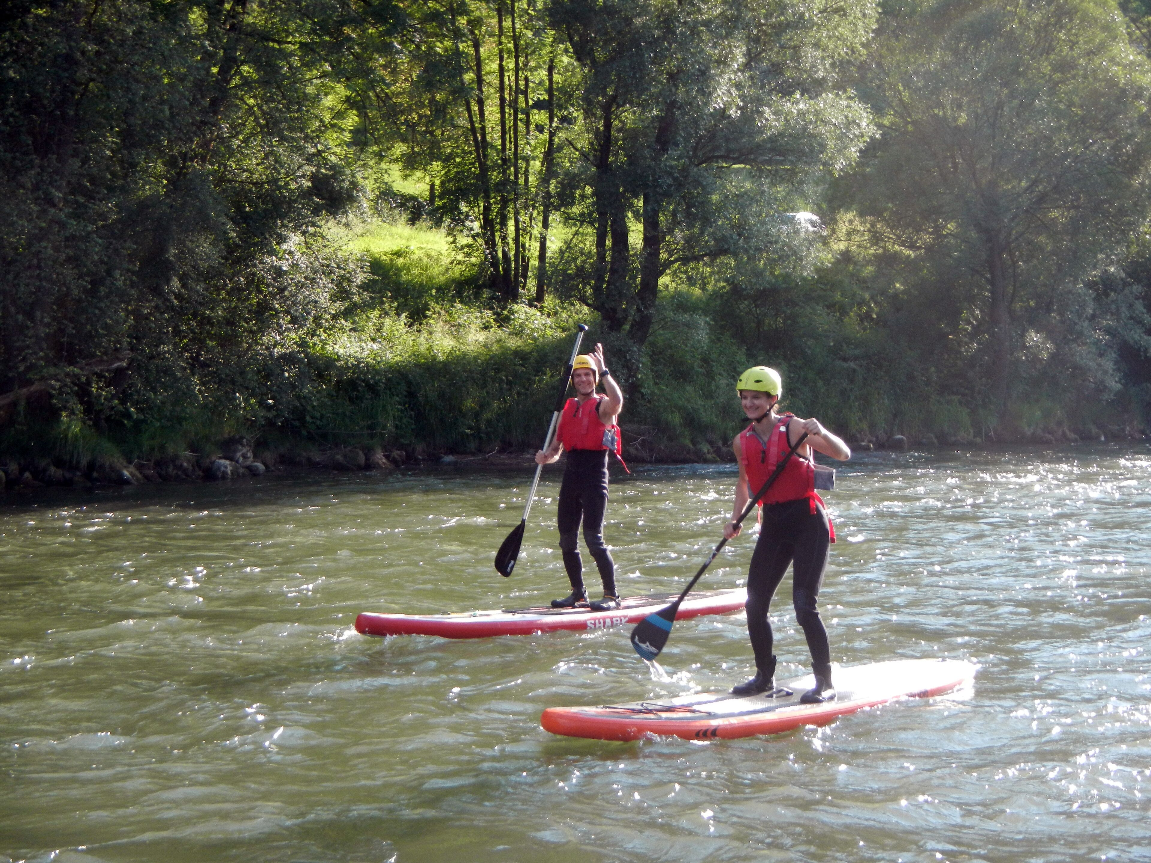 Duas pessoas praticando paddleboard em um rio cercado por árvores.