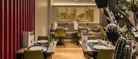 Restaurante com piso de madeira, cadeiras verdes e decoração com cactos.