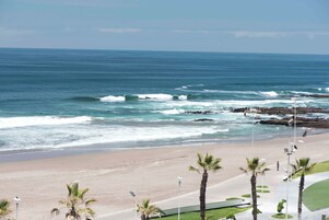 Uma praia com ondas, areal arenoso e palmeiras.
