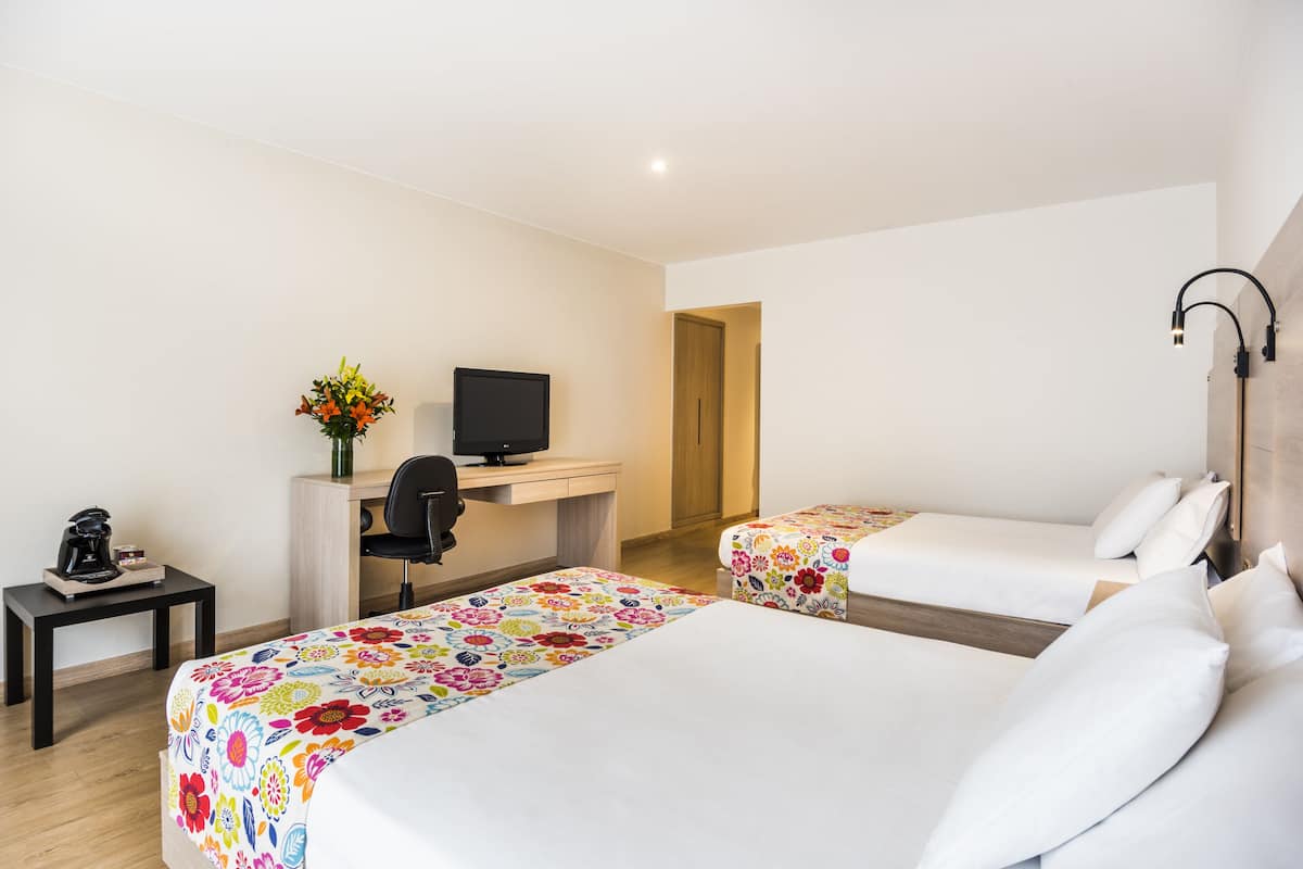 Quarto de hotel com duas camas, uma escrivaninha, uma televisão e uma pequena mesa com cafeteira.