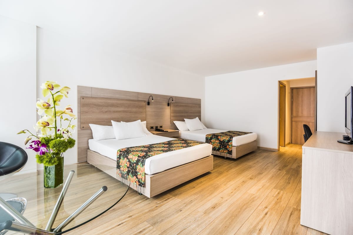 Quarto de hotel moderno com duas camas, uma escrivaninha, uma cadeira e um vaso de flores.