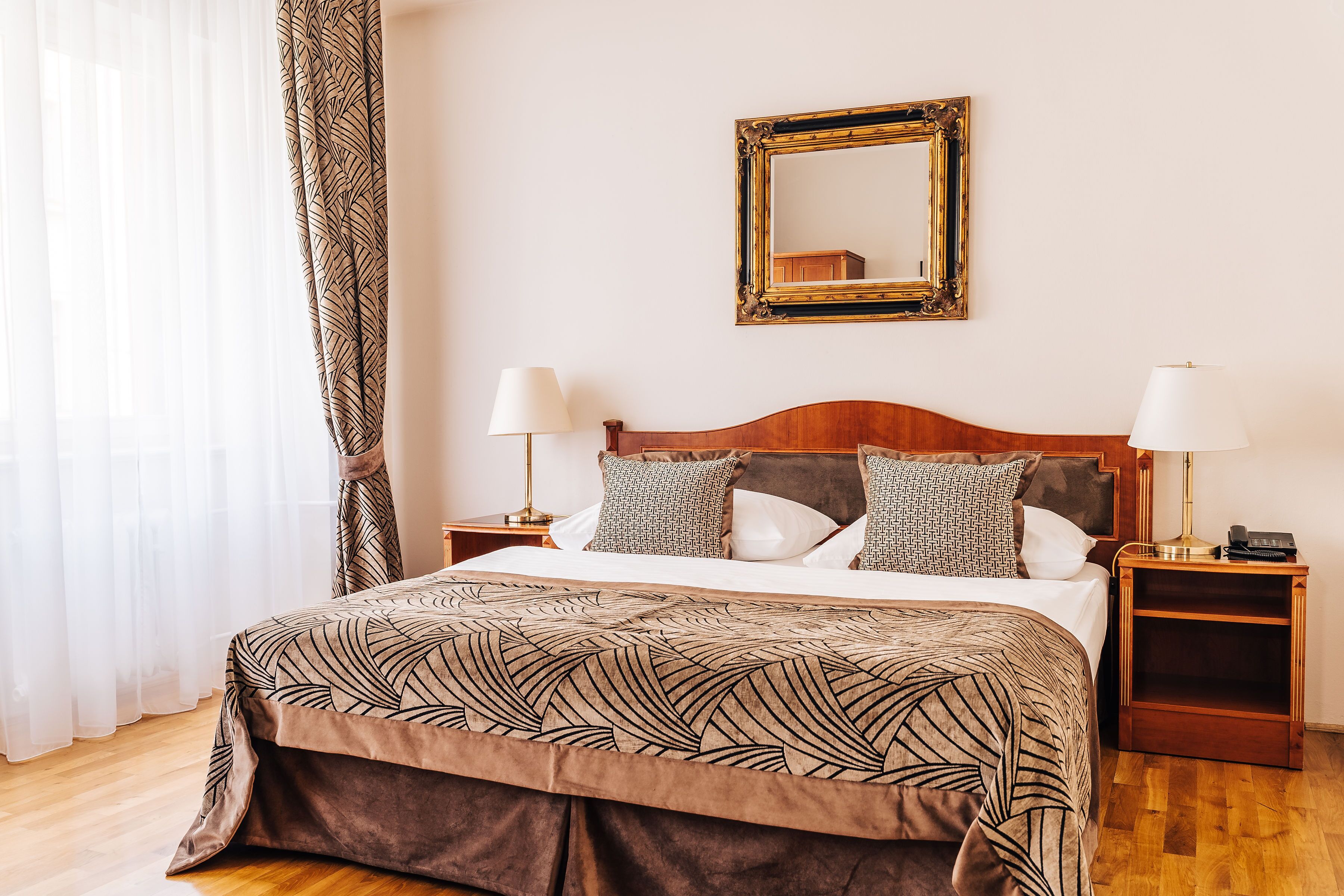 Quarto de hotel com cama, duas mesas de cabeceira, um criado-mudo, luminária, telefone e espelho na parede.