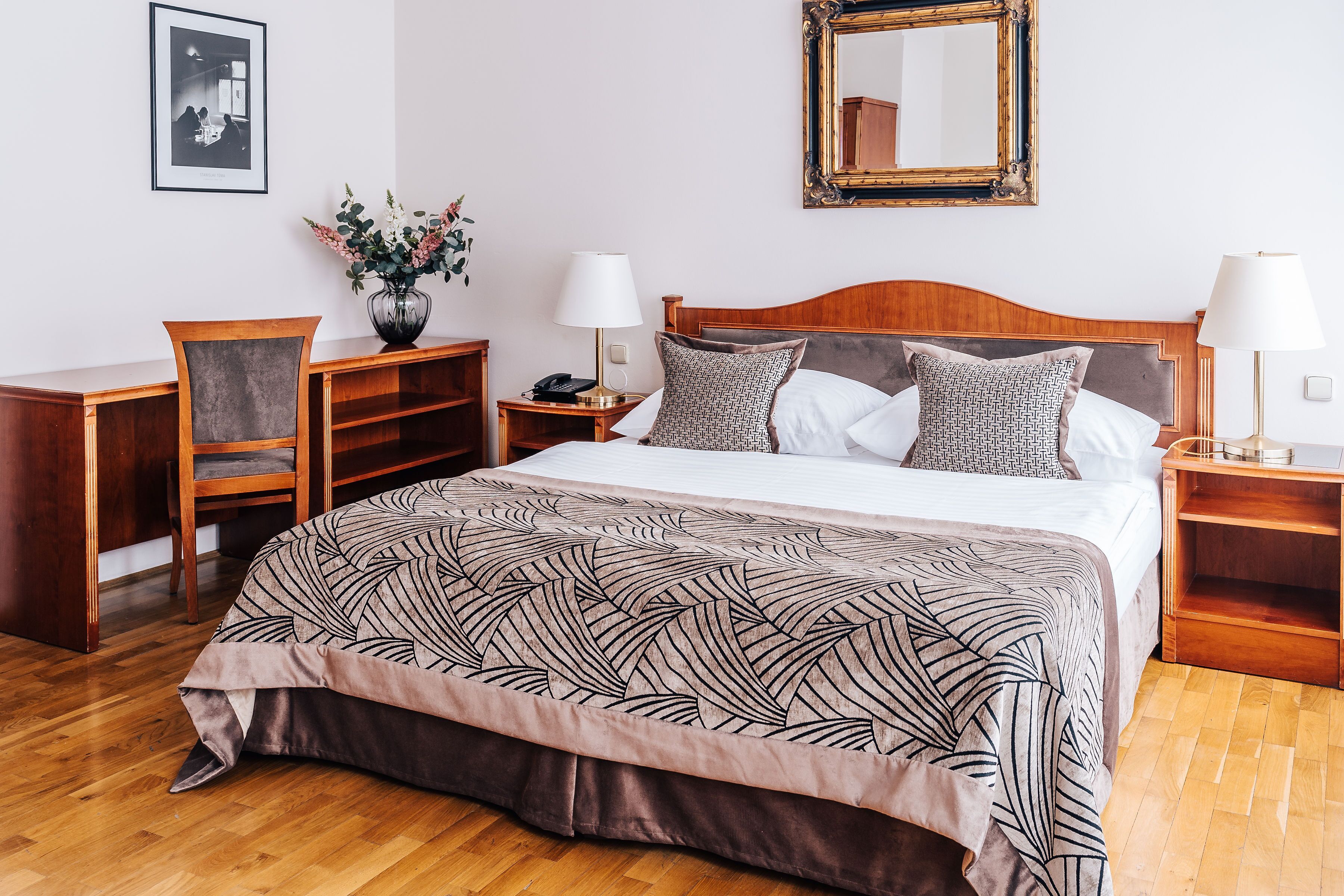 Quarto de hotel bem organizado, com uma cama grande, mesas de cabeceira de madeira, uma escrivaninha e uma cadeira.