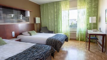 Quarto de hotel com duas camas, uma escrivaninha, uma cadeira e uma janela com cortinas verdes.