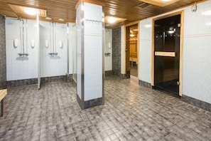 Um banheiro público com piso em azulejos, várias pias e porta de madeira.