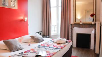 Quarto de hotel com cama, parede vermelha, janela com cortinas, lareira e espelho.