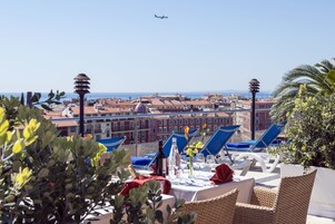 Terraço no telhado com mesas, cadeiras e vista para a paisagem urbana e o mar.