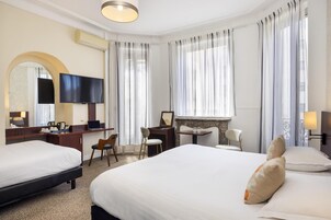 Quarto de hotel com duas camas, uma escrivaninha, uma cadeira, uma televisão e lareira.
