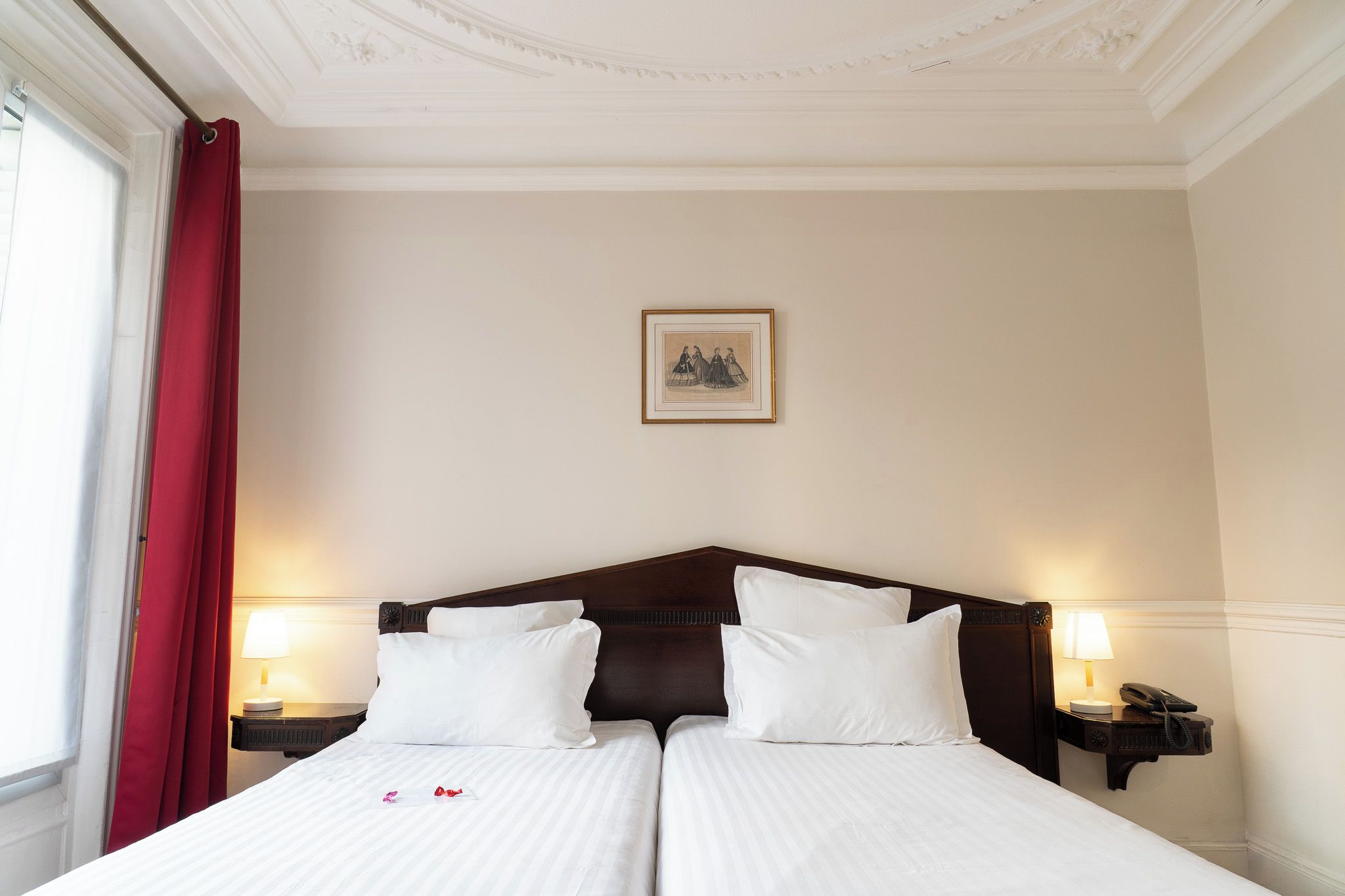 Quarto de hotel com cama de casal, duas luminárias de cabeceira, um quadro na parede e cortina vermelha na janela.