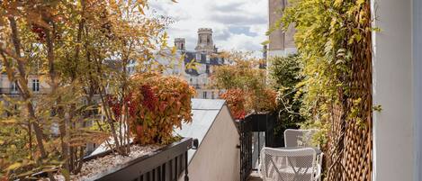 Uma varanda com vista para edifícios, cadeiras de vime branco e plantas.