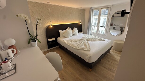 Quarto de hotel moderno com uma cama grande, mesa de cabeceira e escrivaninha com cadeira.
