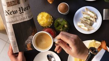 Uma mesa de café da manhã com croissants, geleias, queijo e um jornal.