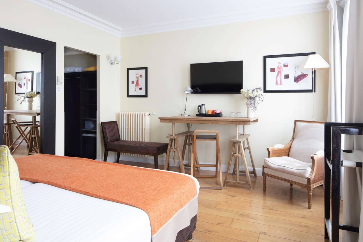Quarto de hotel com cama, escrivaninha, cadeira, televisão e frigorífico.