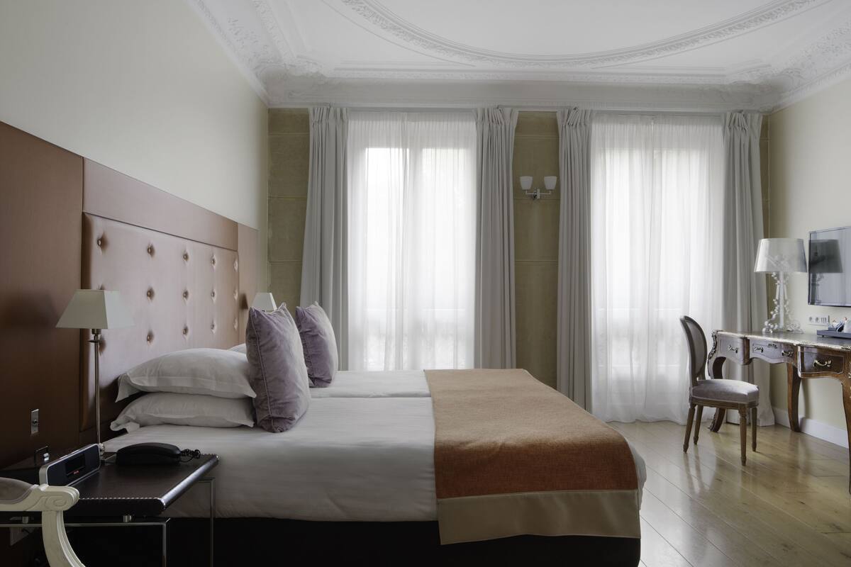 Quarto de hotel com uma cama grande, uma escrivaninha com cadeira, televisão e janela com cortinas.