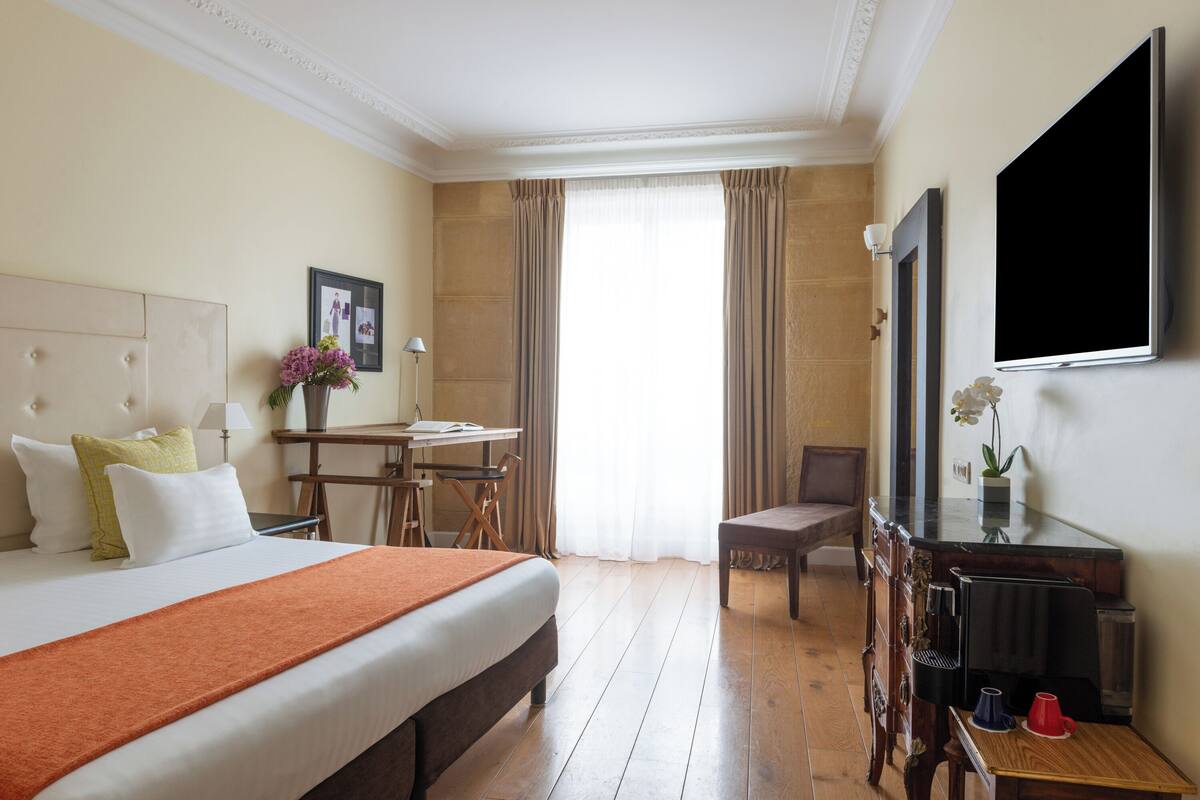 Quarto de hotel com uma cama grande, uma escrivaninha, uma cadeira, uma televisão e uma máquina de café.