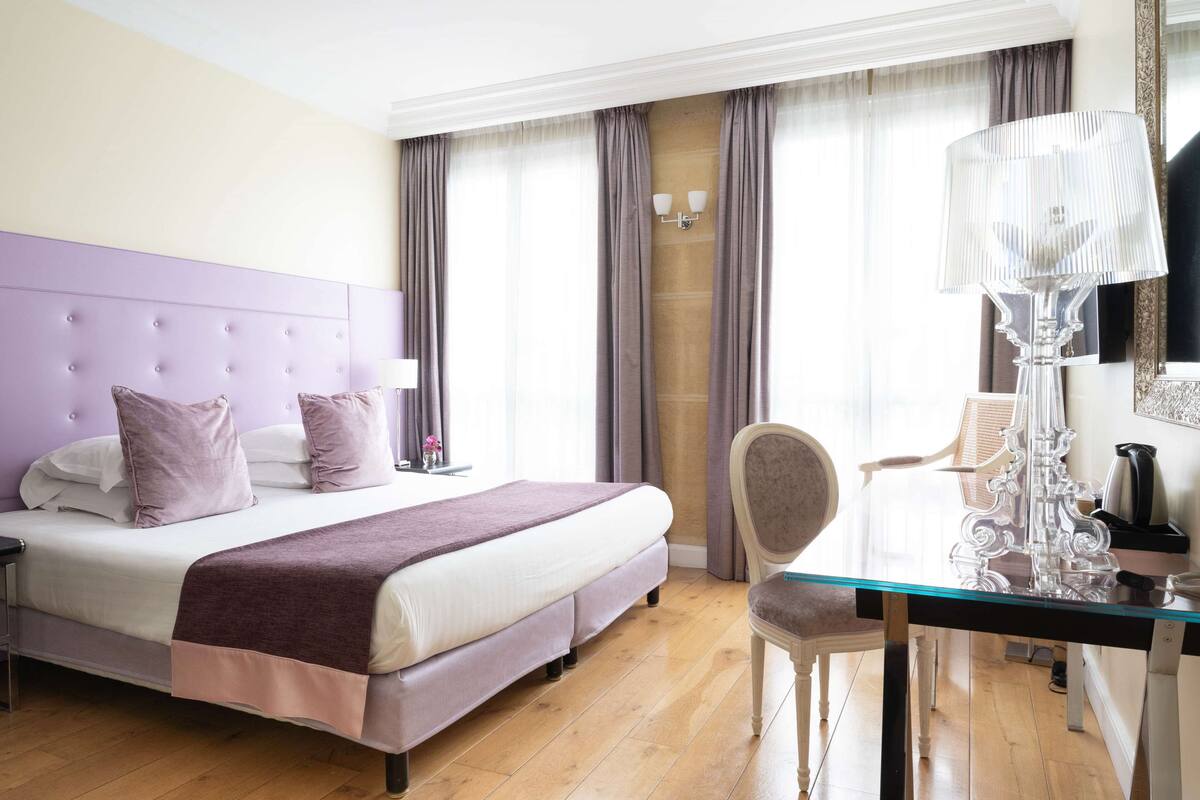 Quarto de hotel com uma cama grande, uma mesa de vidro, uma cadeira, um abajur e um espelho.